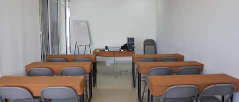 Uma sala de conferências com mesas, cadeiras, um quadro branco e um computador.