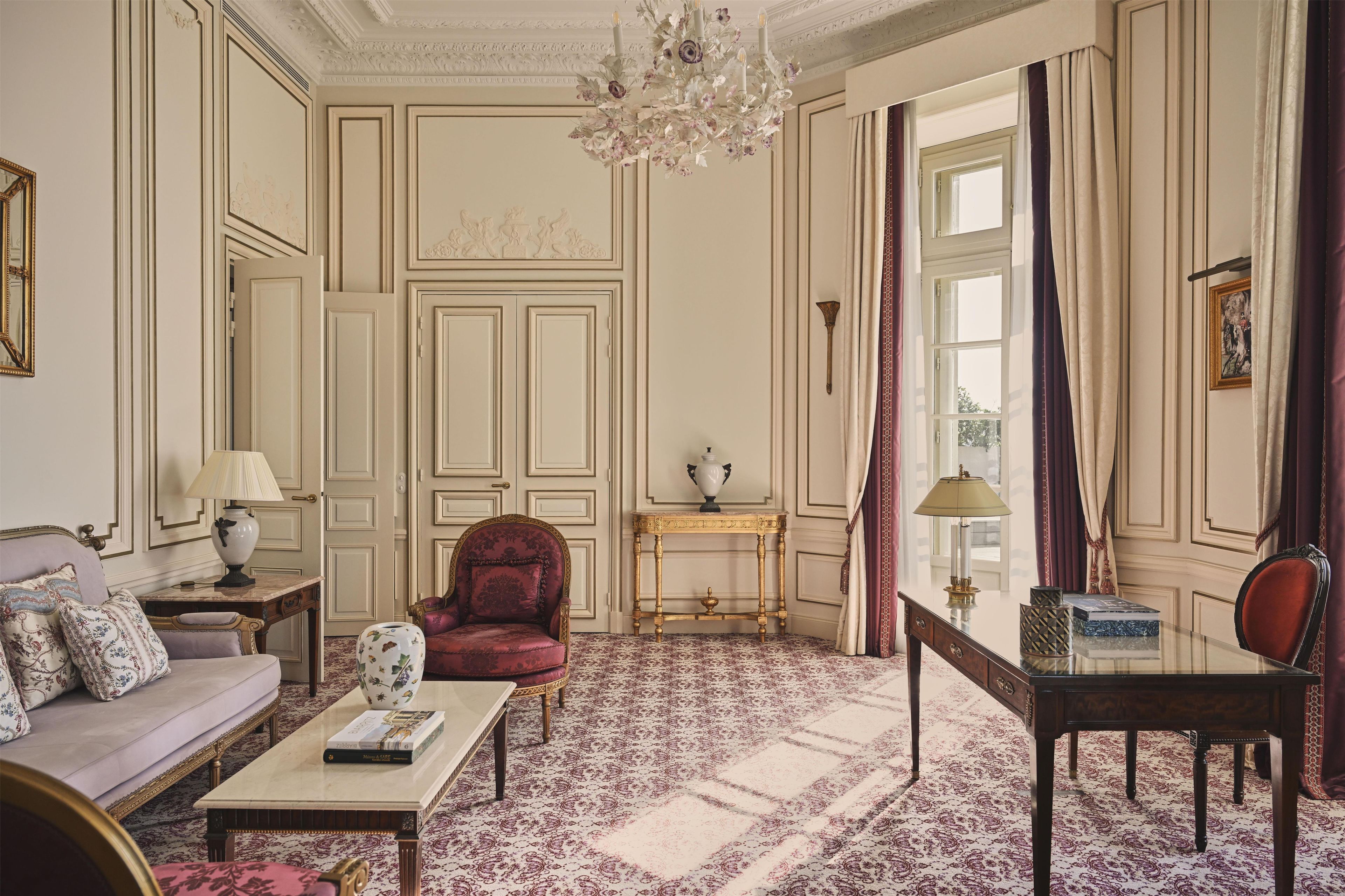 Quarto com sofá, poltrona, mesa e um lustre decorativo.