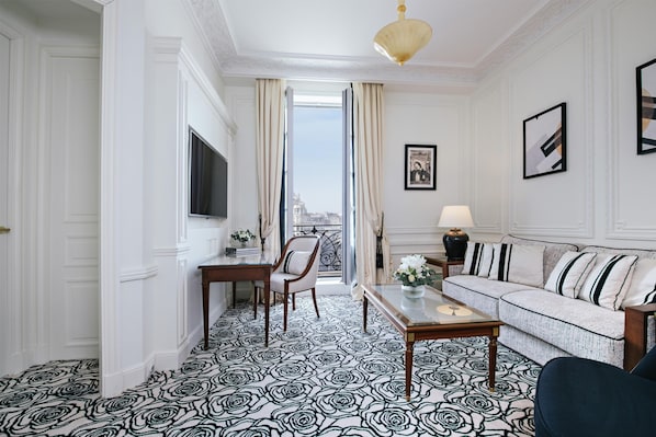 Quarto de hotel com sofá, mesa, cadeira, televisão e piso estampado.