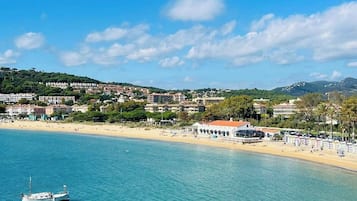 Uma cidade costeira com mar azul cristalino, uma praia arenosa e edifícios ao fundo.