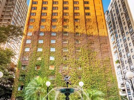 Um edifício com fachada coberta de hera, várias janelas e uma estátua em primeiro plano.