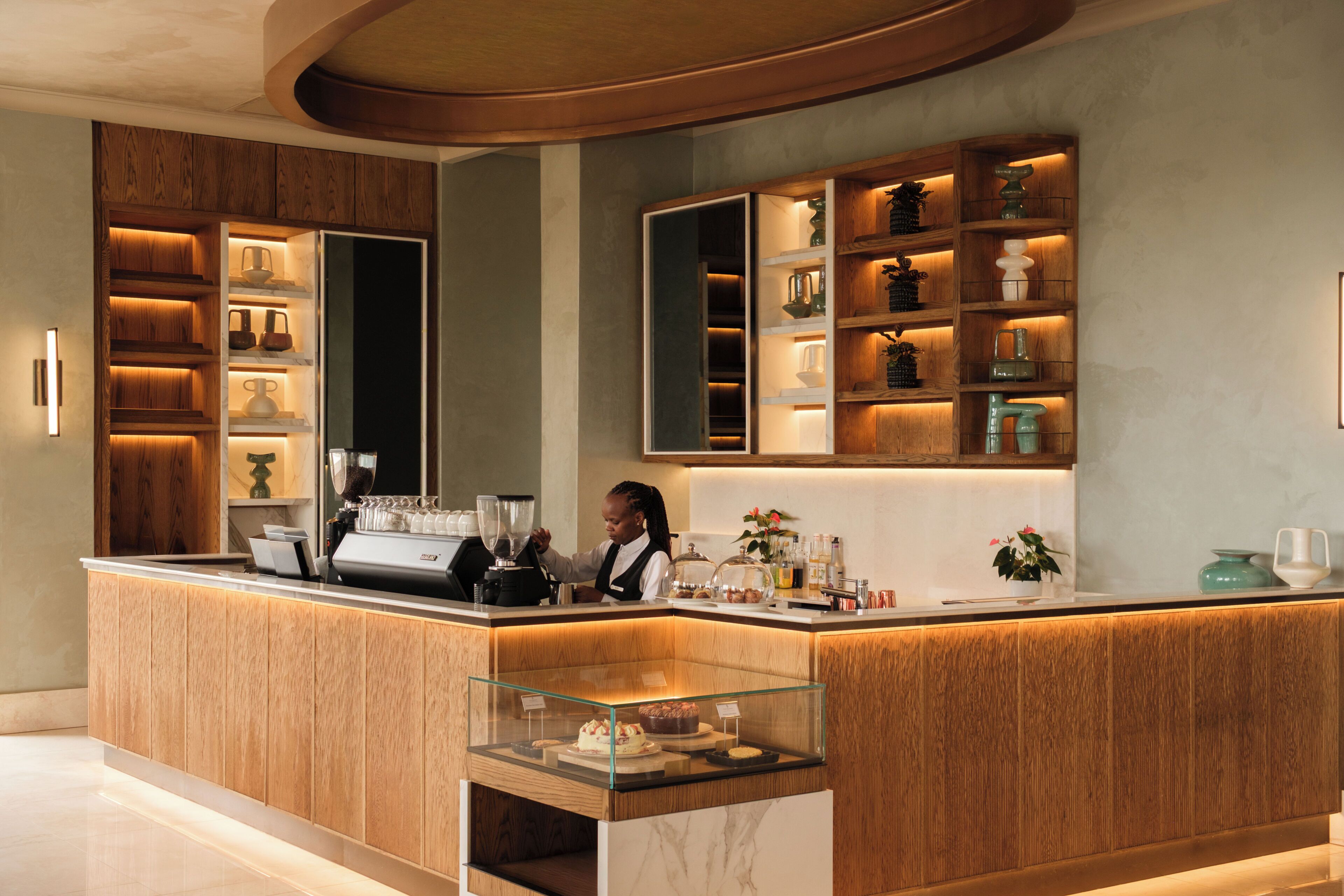Uma área de recepção de hotel moderna, com painéis de madeira, uma vitrine de vidro e uma máquina de café.