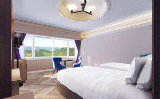 Quarto de hotel com uma cama grande, uma escrivaninha com cadeira e vista para o oceano.