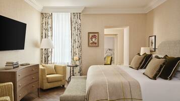 Quarto de hotel com cama, escrivaninha, cadeira, televisão e janela com cortinas.