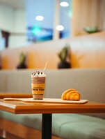 Uma taça de sobremesa com a legenda "Specialty Coffee TOM N TOMS" e um croissant sobre uma mesa de madeira em um café.