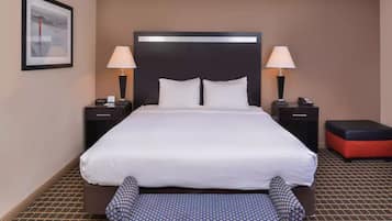 Quarto de hotel com uma cama grande, duas mesas de cabeceira com luminárias, um pequeno banco e um quadro na parede.