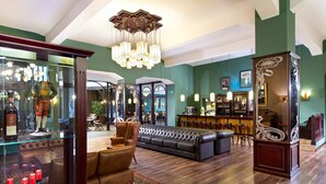 Um hall amplo com sofá de couro, uma vitrine de vidro com garrafas, área de bar em madeira e um grande candelabro.