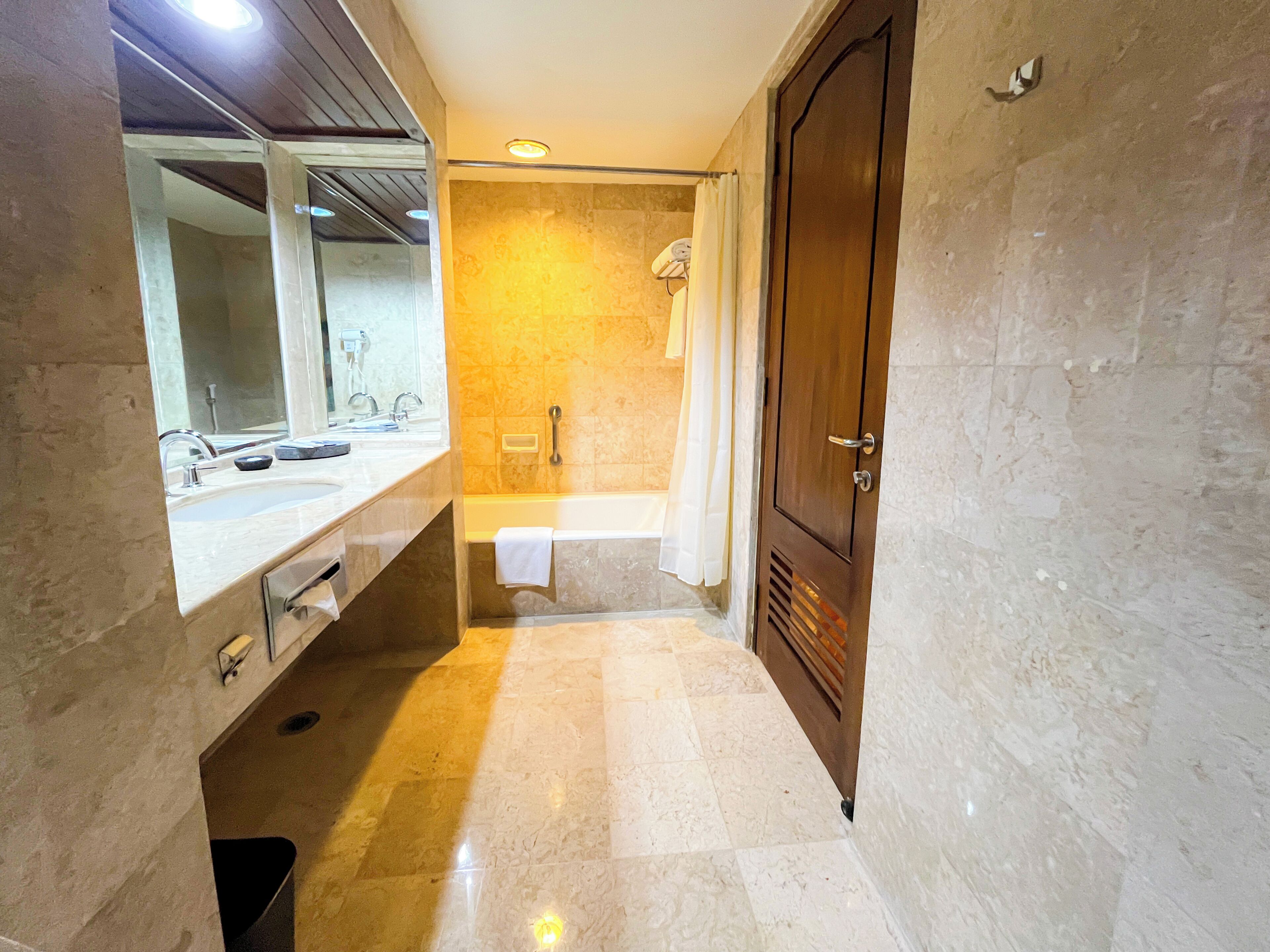 Um banheiro moderno com piso de mármore, um espelho grande, uma banheira e uma porta de madeira.