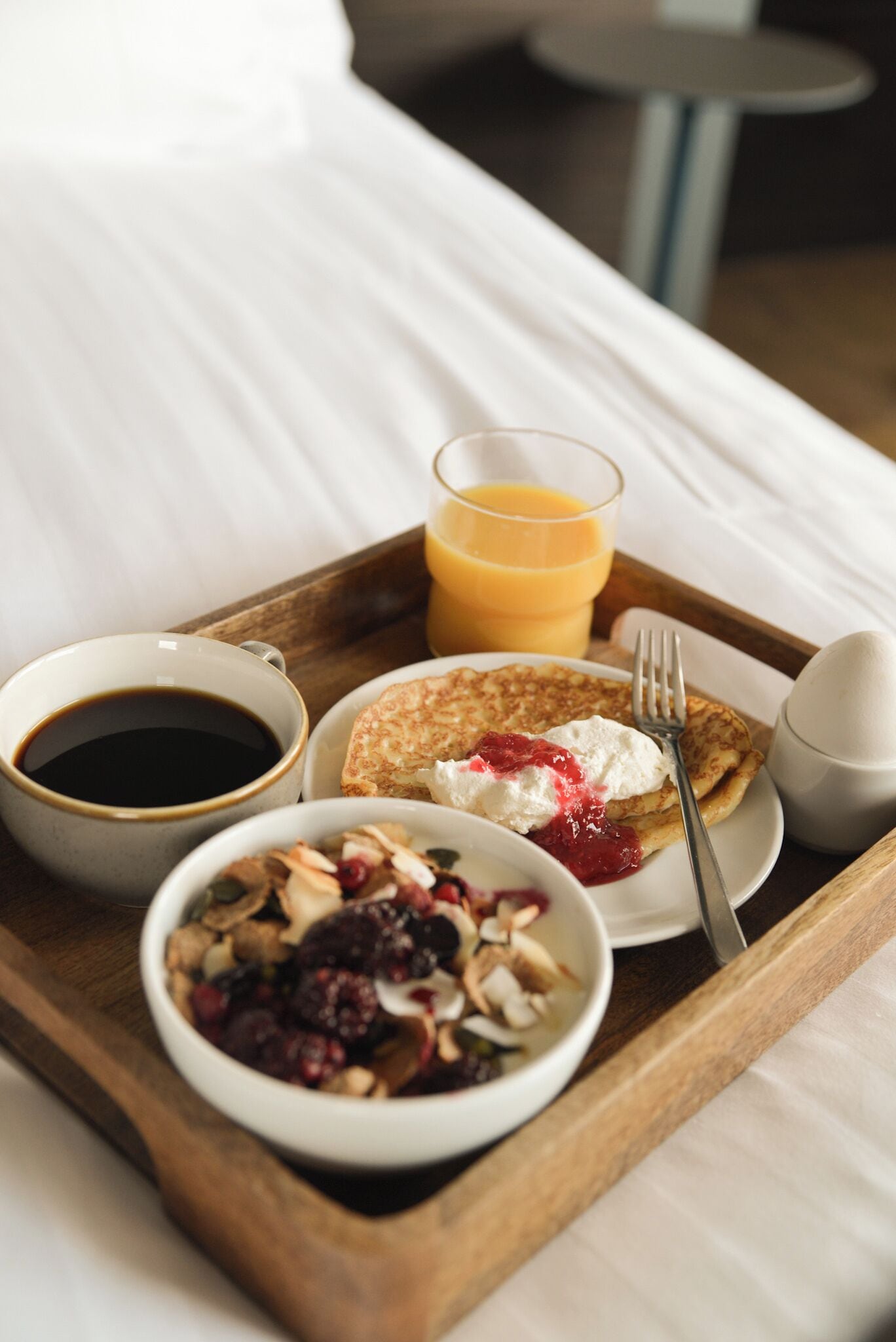 Bandeja de café da manhã com panquecas, frutas vermelhas, iogurte, café e suco de laranja sobre a cama.