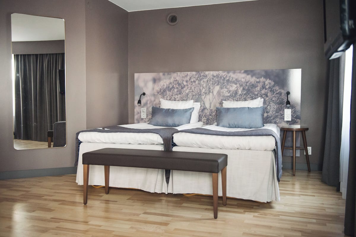 Quarto moderno com uma cama grande, um banquinho, uma mesa de cabeceira e um espelho.