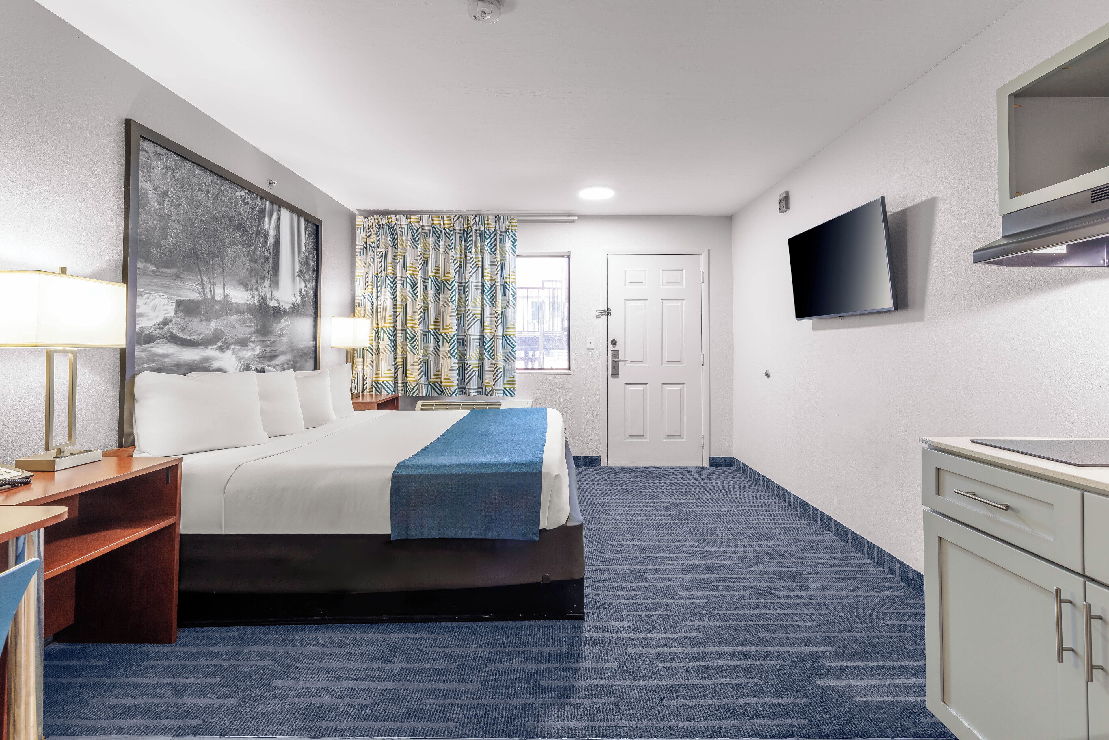 Quarto de hotel com cama, escrivaninha, televisão e armário de banheiro.