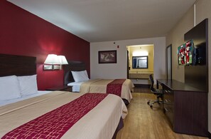 Quarto de hotel com duas camas, uma escrivaninha, uma cadeira, televisão e banheiro ao fundo.