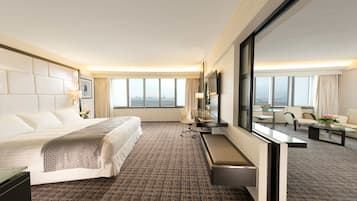 Quarto de hotel moderno com uma cama grande, uma escrivaninha, uma cadeira e vista da cidade por grandes janelas.