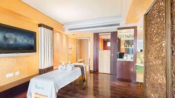 Quarto de hotel com mesa de massagem, televisão na parede e painel decorativo.