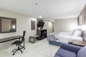 Quarto de hotel moderno com cama, escrivaninha, cadeira e televisão.
