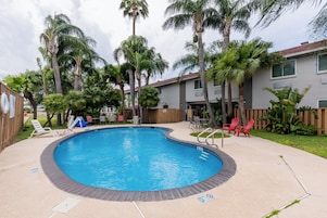 Piscina com borda de tijolos, rodeada por palmeiras e um cercado de madeira.
