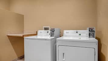 Duas máquinas de lavar Whirlpool de abertura frontal numa lavanderia com paredes bege e uma prateleira de madeira.