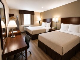 Quarto de hotel com duas camas, uma escrivaninha, uma cadeira, um abajur e um espelho.