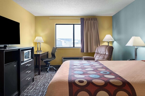 Quarto de hotel com cama, escrivaninha, cadeira, televisão e janela com cortinas.