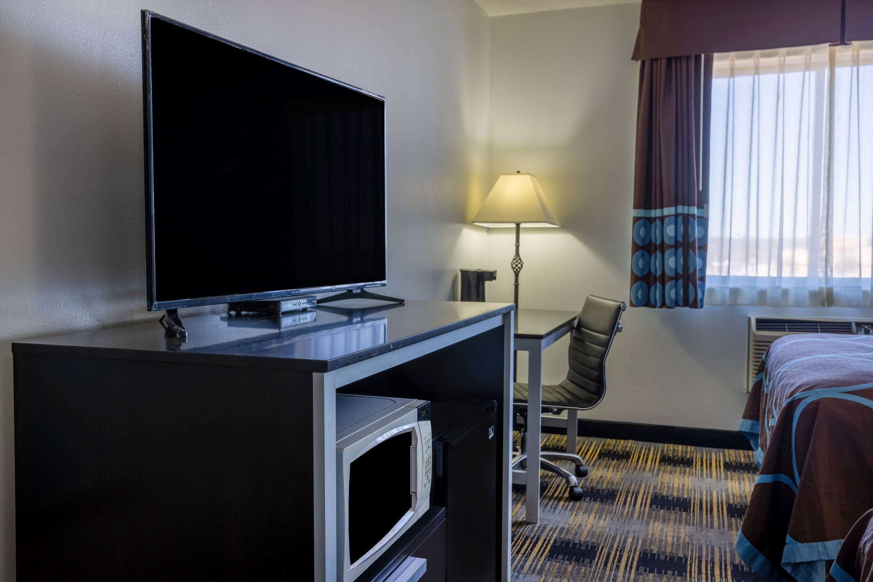 Quarto de hotel com televisão de tela plana em uma mesa, luminária, cama e carpete estampado.