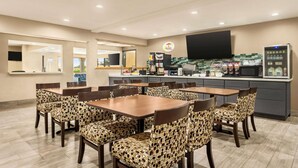 Um restaurante com uma mesa comprida e cadeiras, um balcão com uma máquina de café e uma televisão fixada na parede.