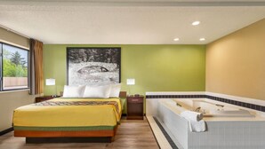 Quarto de hotel com cama, uma janela grande, um quadro, banheiro com banheira e mesa de cabeceira.