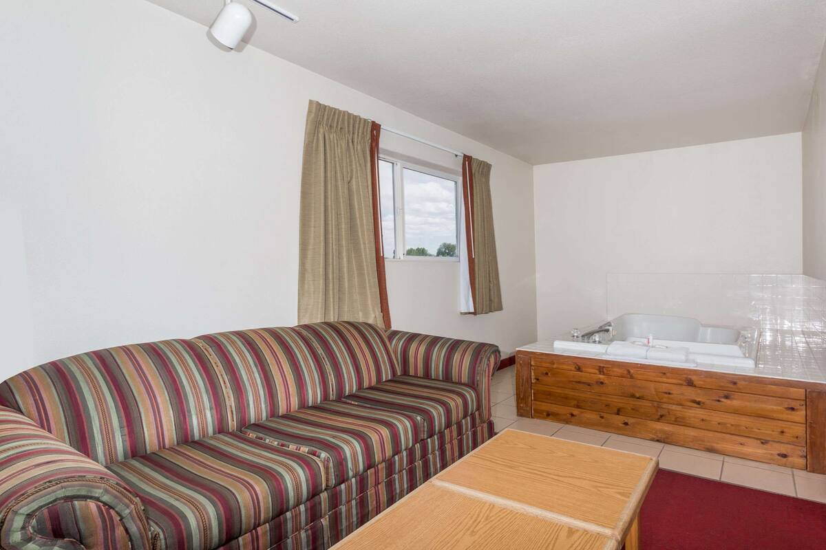 Um quarto com um sofá listrado, uma mesa de madeira, um armário de madeira e uma janela com cortinas.