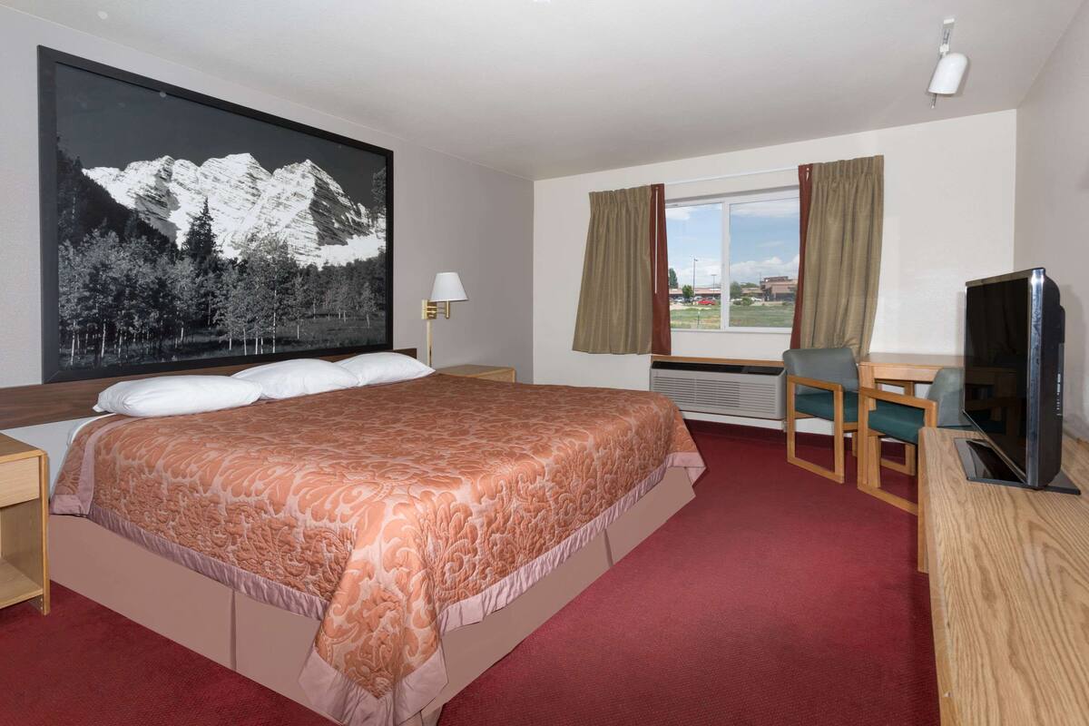 Quarto de hotel com uma cama grande, uma escrivaninha, uma cadeira, uma televisão e uma janela com cortinas.