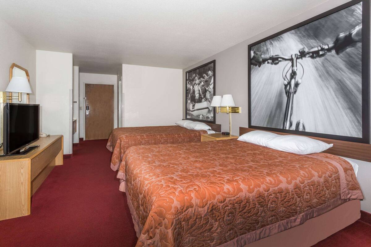 Quarto de hotel com duas camas, televisão, escrivaninha e um quadro grande na parede.