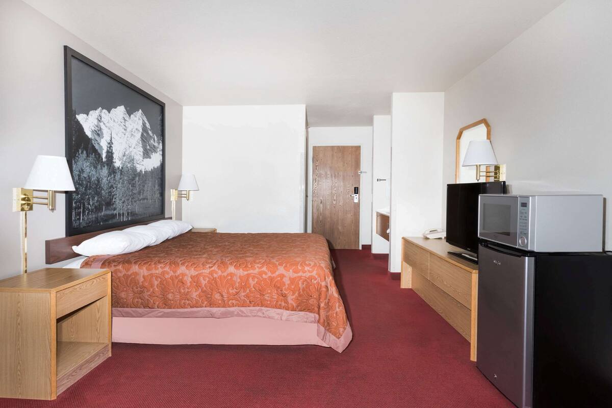 Quarto de hotel com cama, televisão, frigorífico e um quadro grande emoldurado na parede.