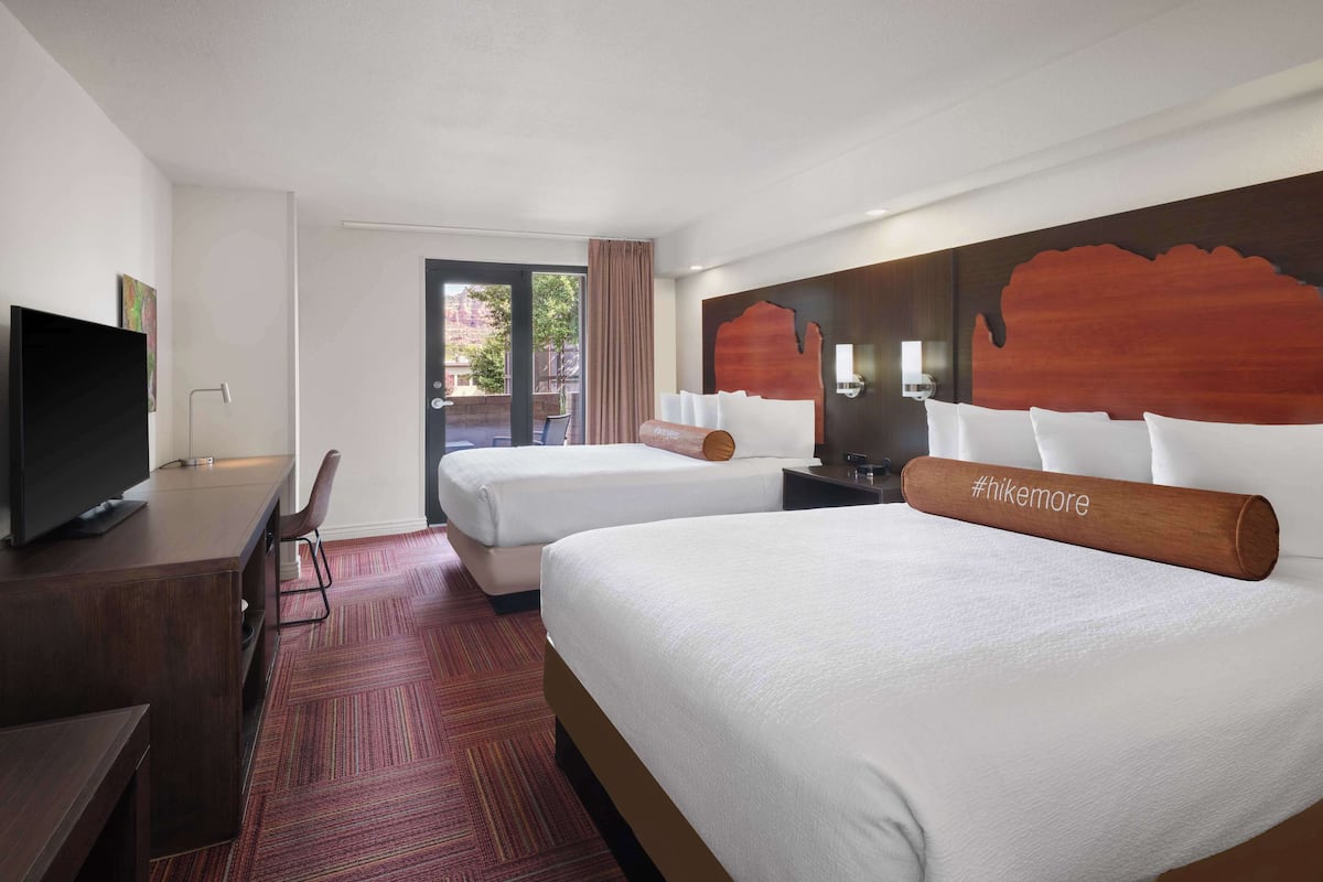 Quarto de hotel com duas camas, uma escrivaninha, televisão e uma janela grande.