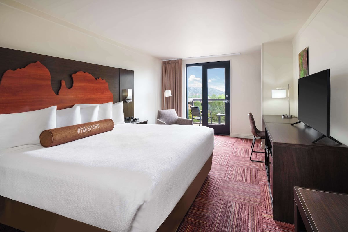 Quarto de hotel com uma cama grande, uma mesa, uma cadeira, uma televisão e uma varanda com vista.