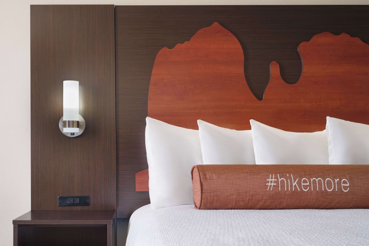 Quarto de hotel com cabeceira de madeira, roupa de cama branca e travesseiro #hikemore.