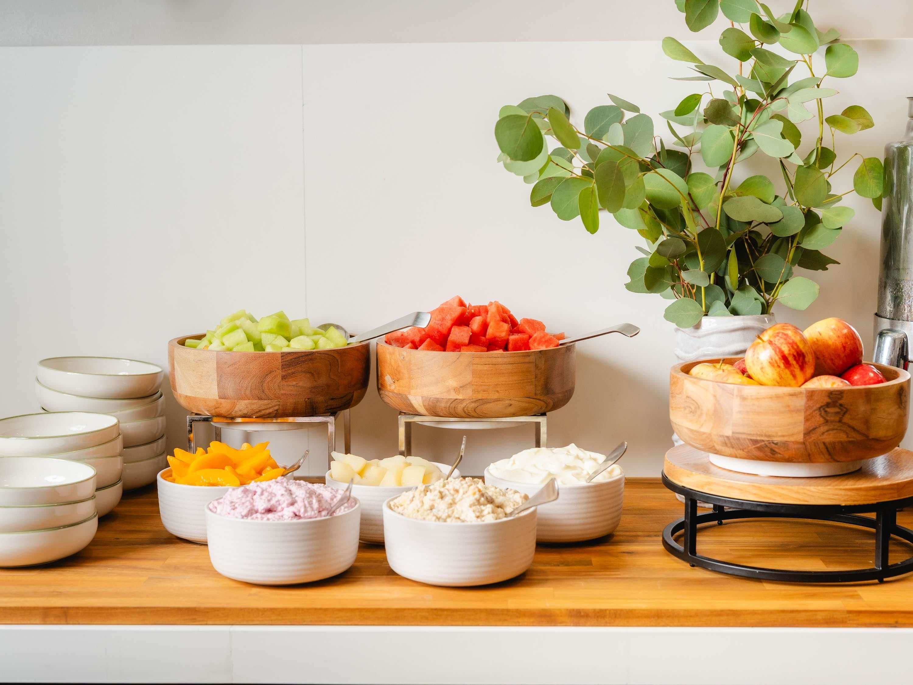 Uma mesa de buffet com diversos alimentos em recipientes, incluindo frutas, legumes e molhos.