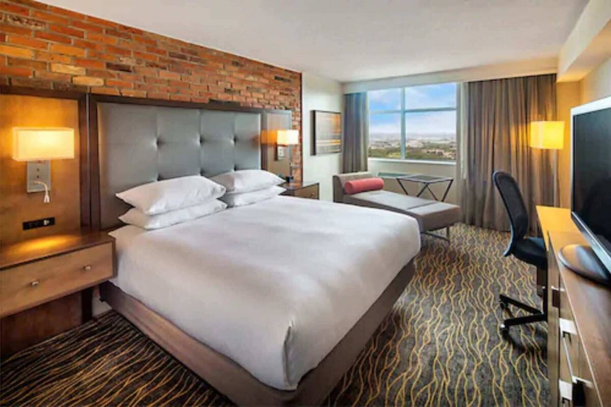 Quarto de hotel com cama grande, escrivaninha, cadeira, televisão e vista para a cidade.