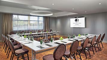Uma sala de conferências com uma mesa comprida, cadeiras e uma tela exibindo o logotipo DoubleTree by Hilton.