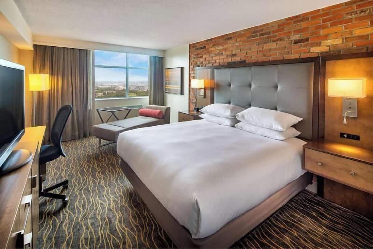 Quarto de hotel com uma cama grande, uma escrivaninha, uma cadeira, uma televisão e vista para a cidade.