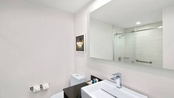 Uma casa de banho moderna com uma sanita, um lavatório branco e um chuveiro com cabine de vidro.