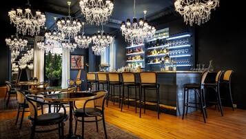 Uma área de bar com vários lustres, mesas de madeira e banquetas de bar pretas.