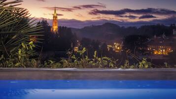 Vista de um campanário de igreja ao entardecer, com edifícios e vegetação ao redor.