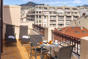 Varanda com duas cadeiras, uma mesa com café da manhã e vista para a cidade.