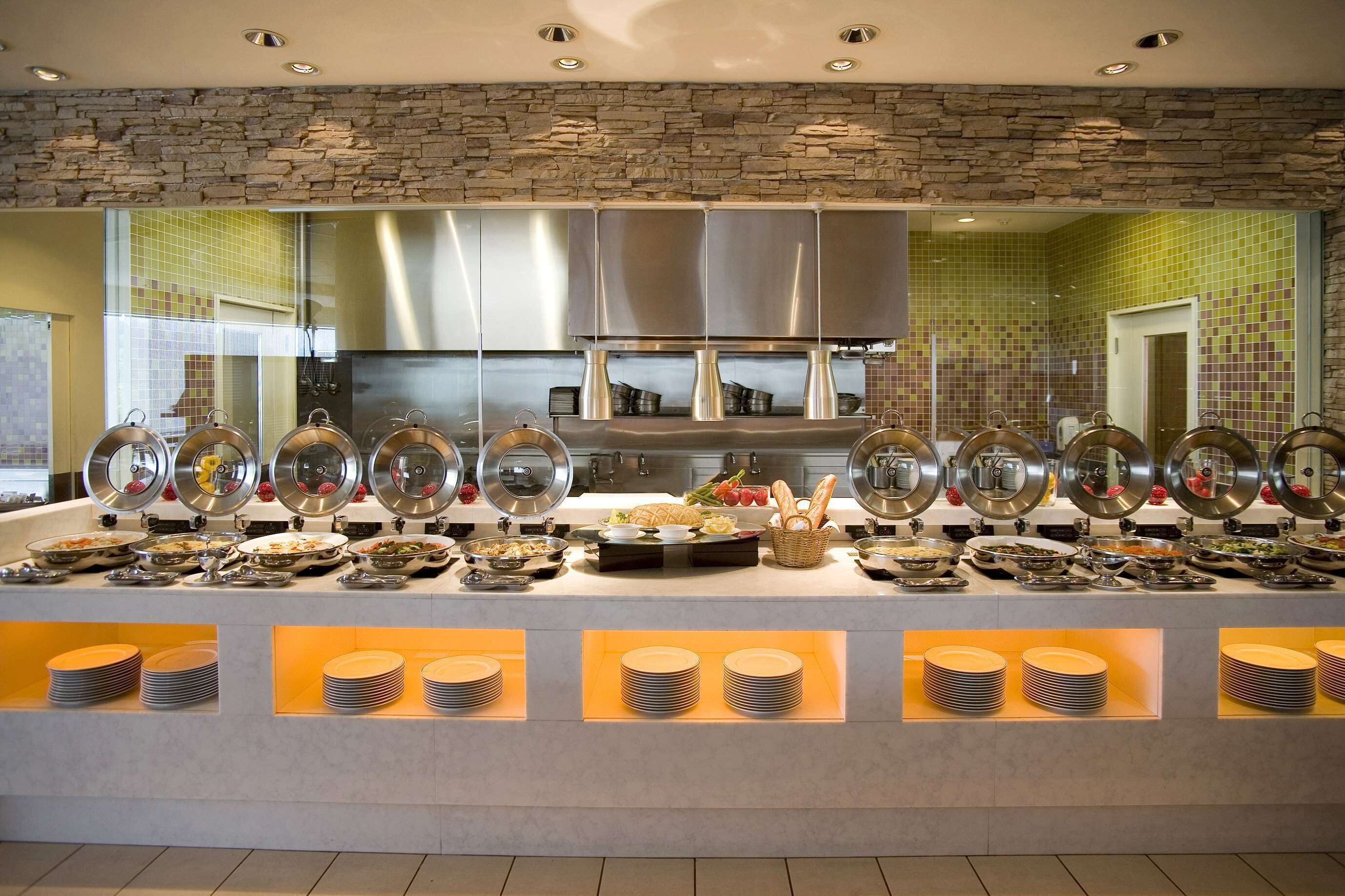 Buffet montado com diversas estações de serviço, uma parede de pedra e uma área de cozinha ao fundo.