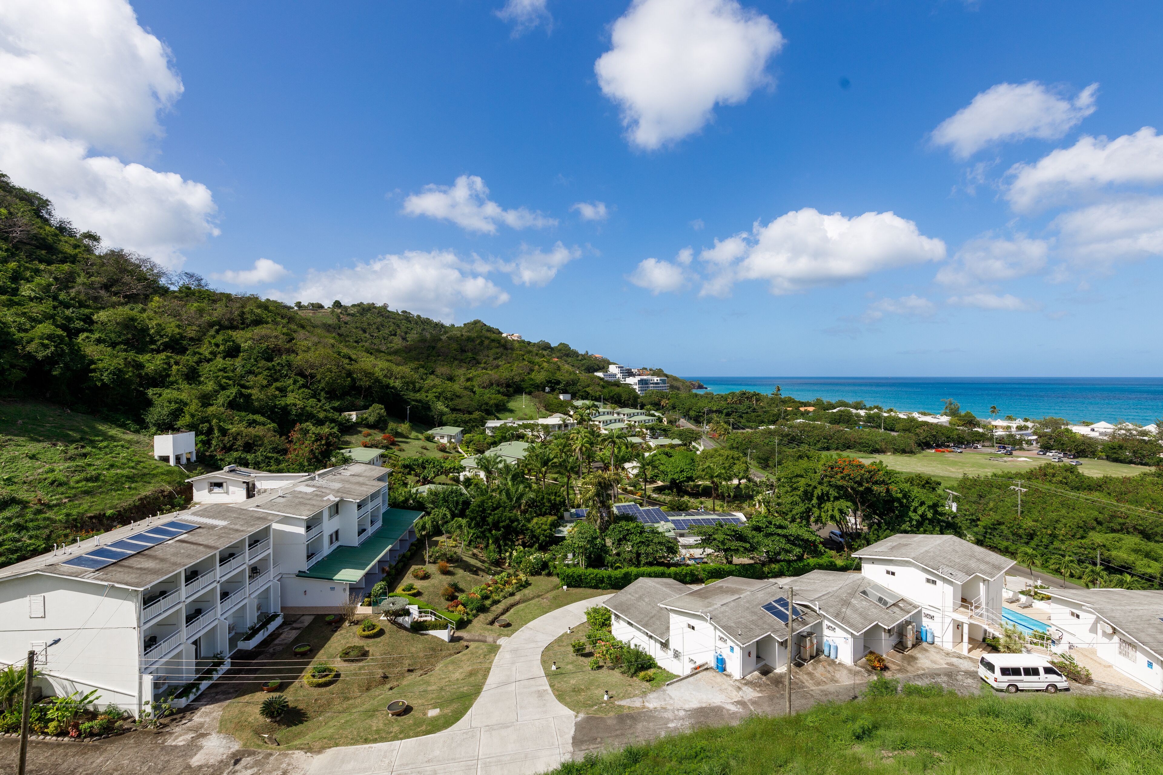 Um resort costeiro com vários edifícios, vista clara do oceano e vegetação exuberante.