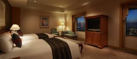 Quarto de hotel com duas camas, televisão, escrivaninha e janela com vista para a cidade.