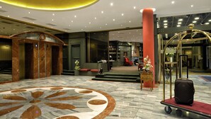 Um hall com piso de mármore, balcão de recepção, área de estar e escada que leva a outro andar.