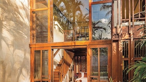 Um interior espaçoso com uma escada que leva a um andar superior, uma área de estar aconchegante com almofadas e uma grande planta em vaso.