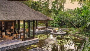 Construção com telhado de palha, mesas ao ar livre e um lago com nenúfares.