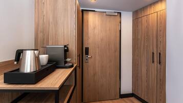 Quarto de hotel moderno com um guarda-roupa de madeira, um espaço para café e uma porta com puxador.