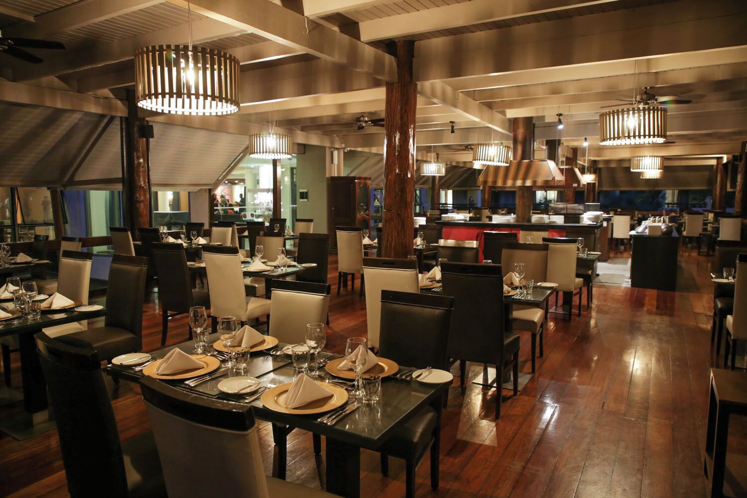 Um restaurante com várias mesas, cadeiras e luminárias pendentes.