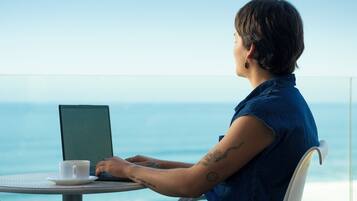 Uma pessoa à mesa com um laptop e uma xícara, com vista para a água.